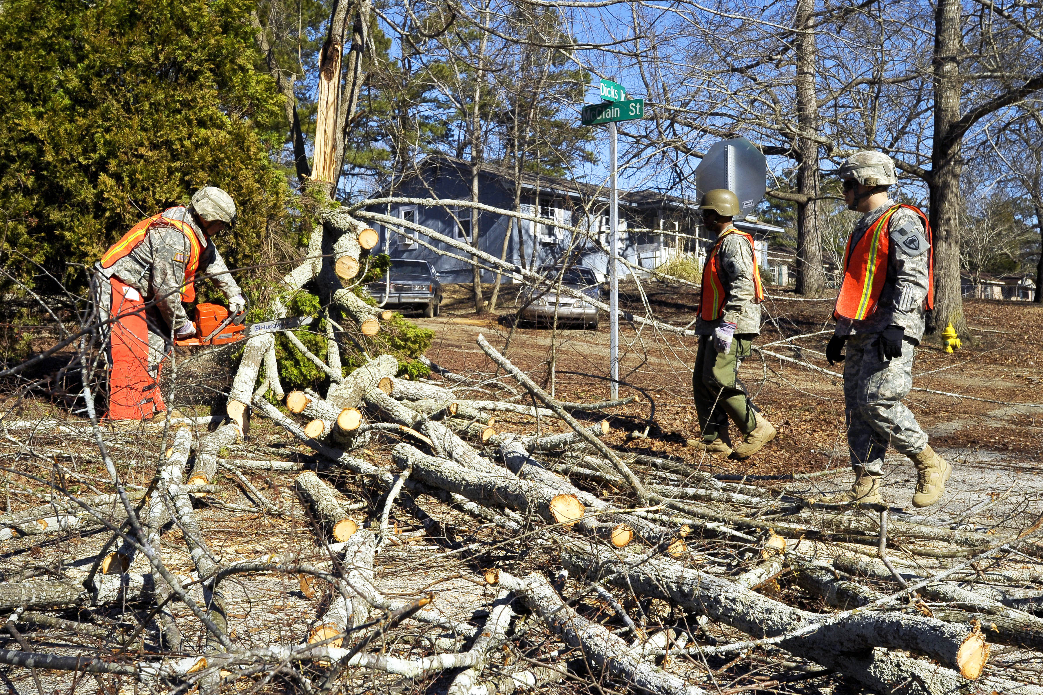 A soldier uses a chain saw to cut away tree branches as other soldiers ...