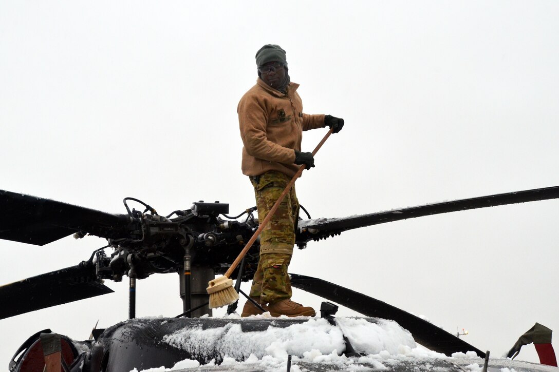 U.S. Army Spc. Jimmy Rop uses a push broom to remove snow from a UH-60 ...