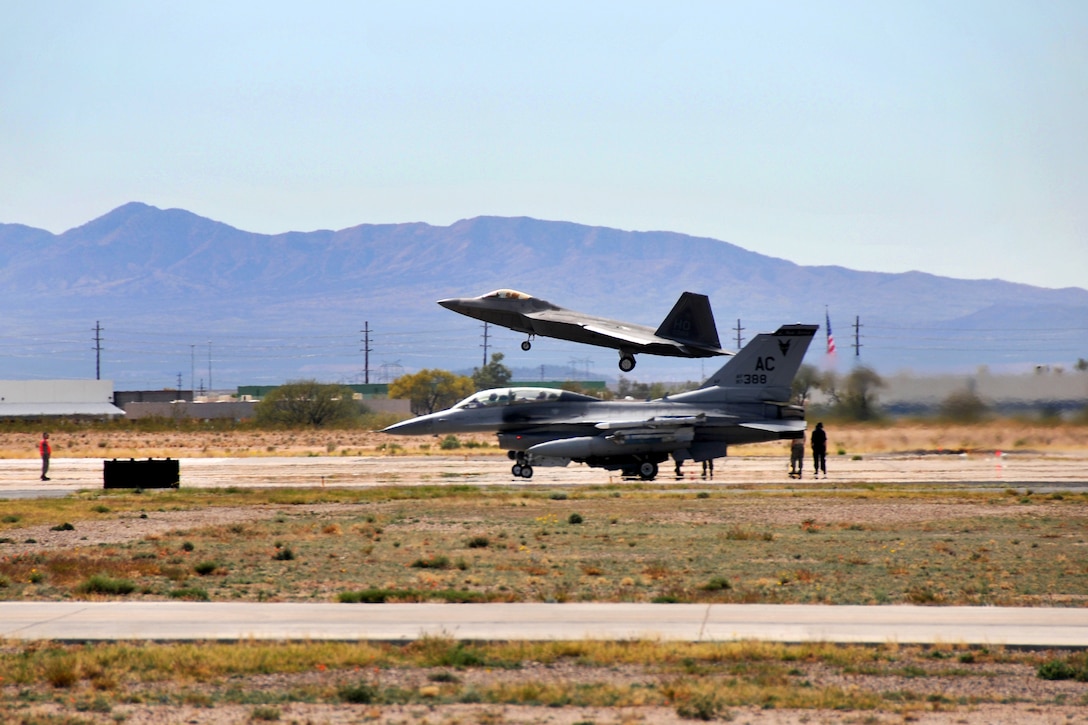 An F-22 Raptor makes a landing approach as two F-16 Fighting Falcons ...
