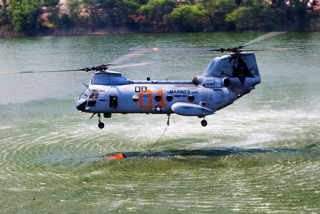 A Marine Corps CH-46 Sea Knight helicopter fills a Bambi bucket to help ...