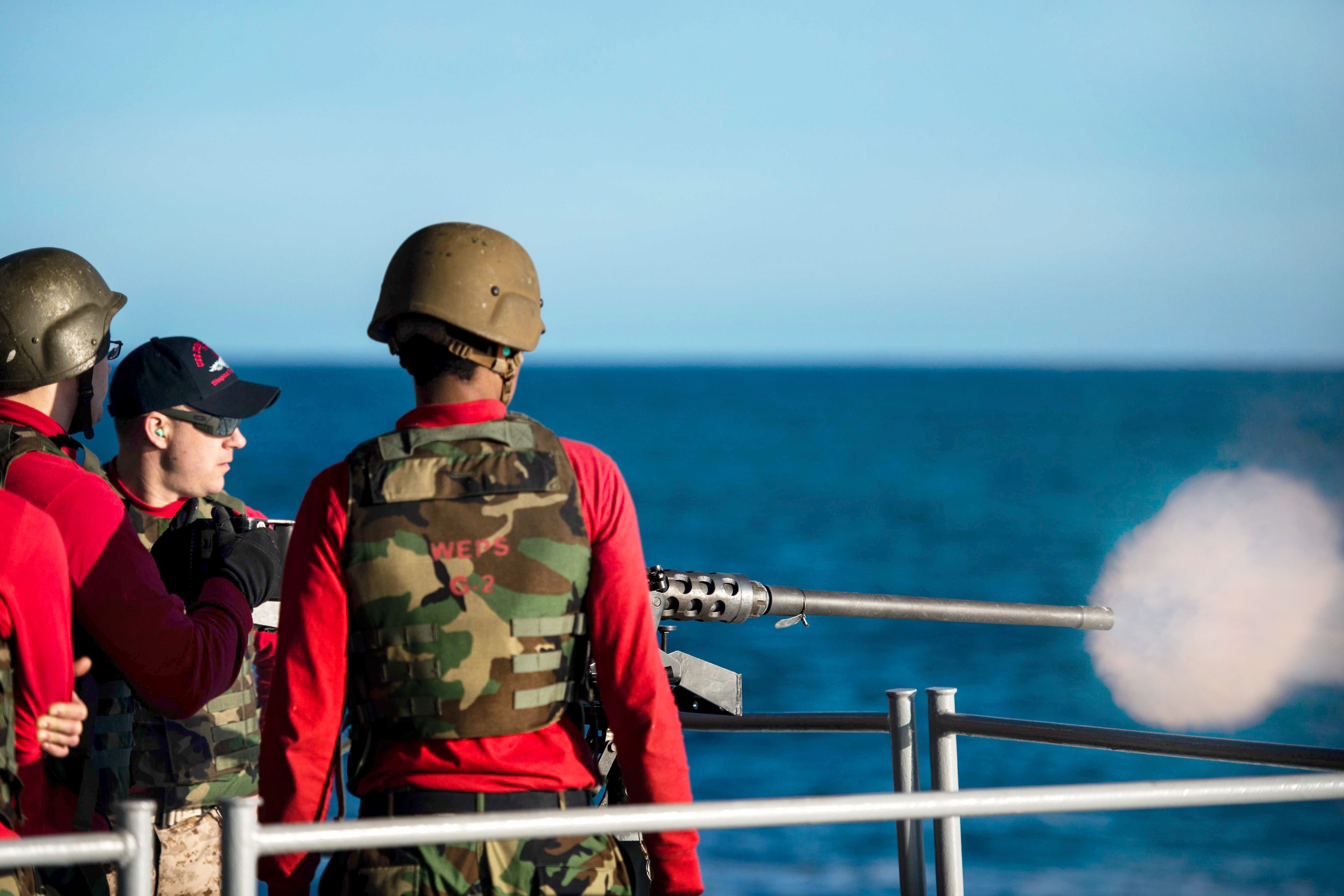 Sailors fire a .50-caliber gun on the fantail of the Nimitz-class ...