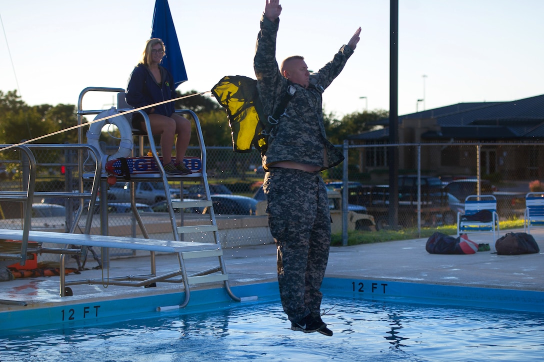 A soldier jumps from a diving board into a pool while wearing a ...