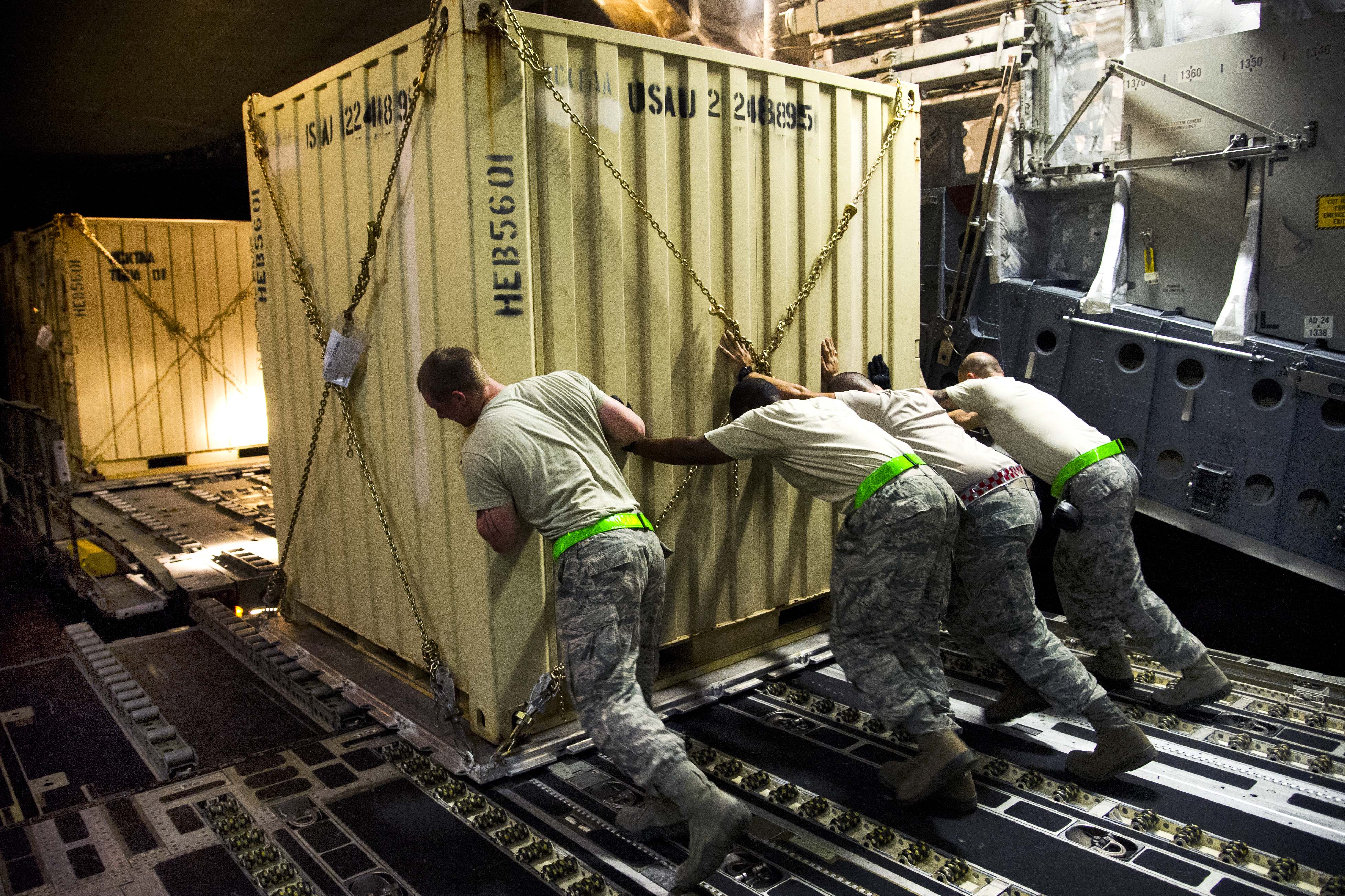 U.S. airmen push a cargo pallet off of a C-17 Globemaster III aircraft ...