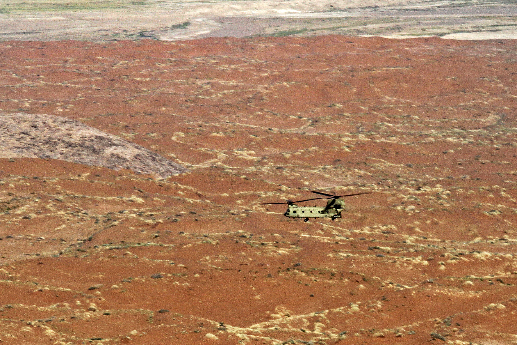 A U.S. CH-47F Chinook helicopter flies over the red desert in southern ...
