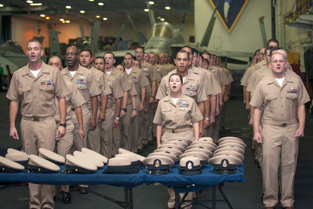 U.S. Navy chief petty officers stand in ranks singing "Anchors Aweigh ...