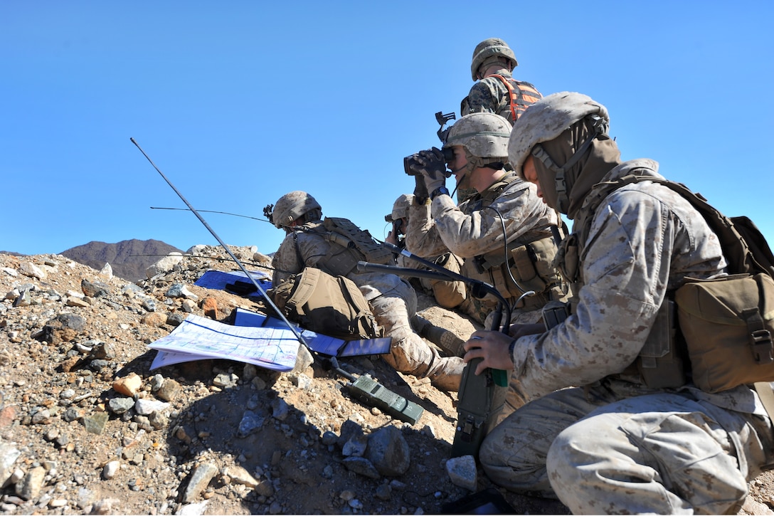 A Marine scans the area using binoculars as other Marines look over a ...