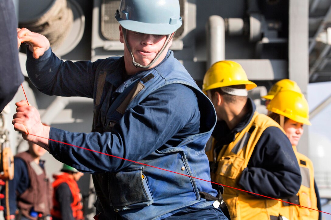 U.S. Navy Seaman Trevor Herbert, foreground, brings in line aboard the ...