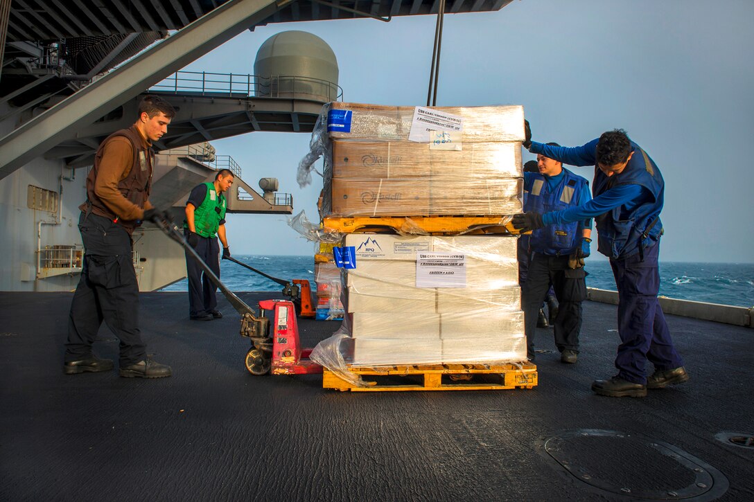U.S. sailors transport cargo onto an aircraft elevator aboard the ...