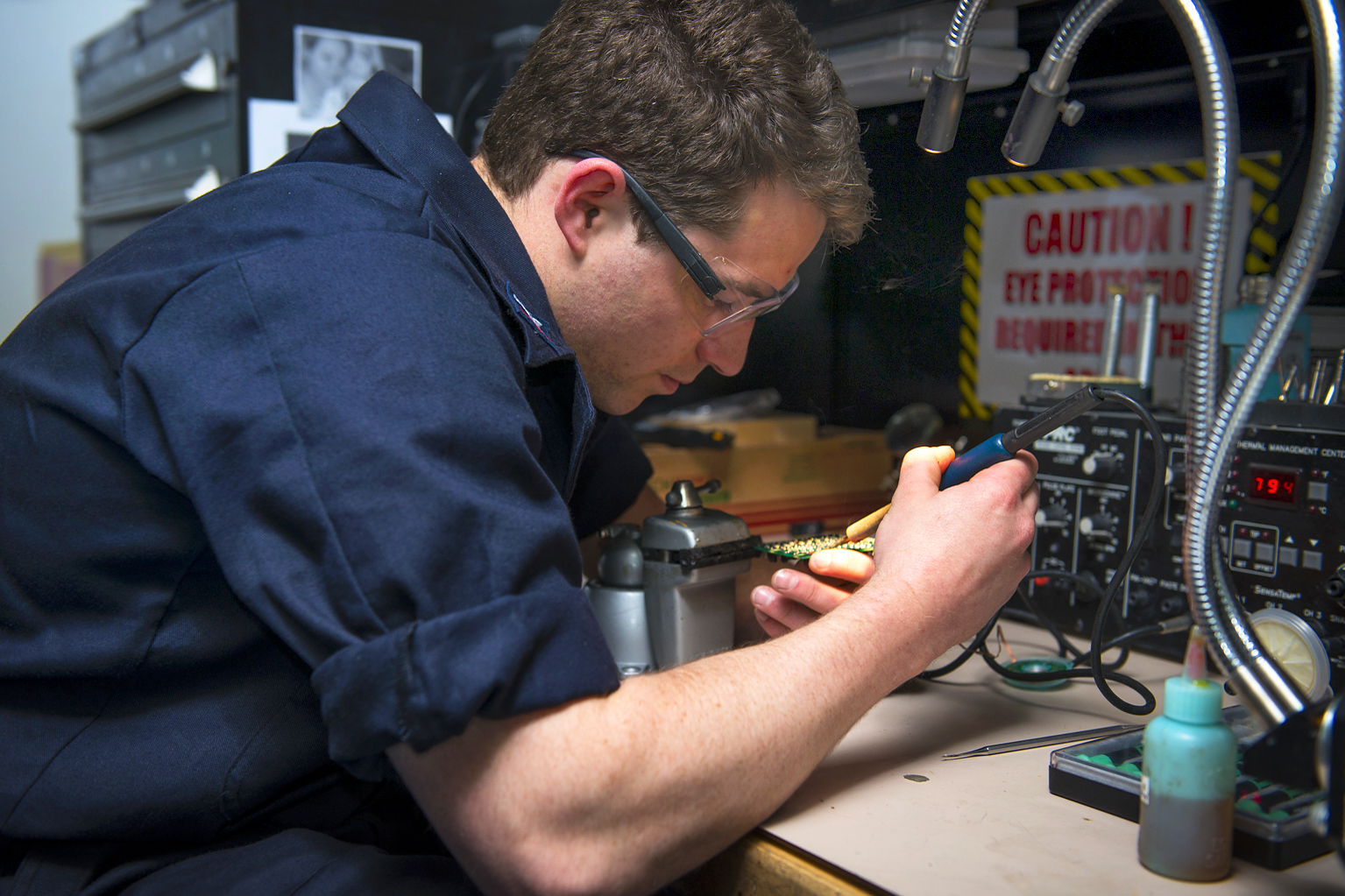 U.S. Navy Petty Officer 3rd Class Marley Camden repairs a circuit board ...