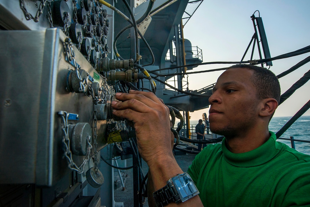 U.S. Navy Petty Officer Steve Smith connects cables on the fantail of ...