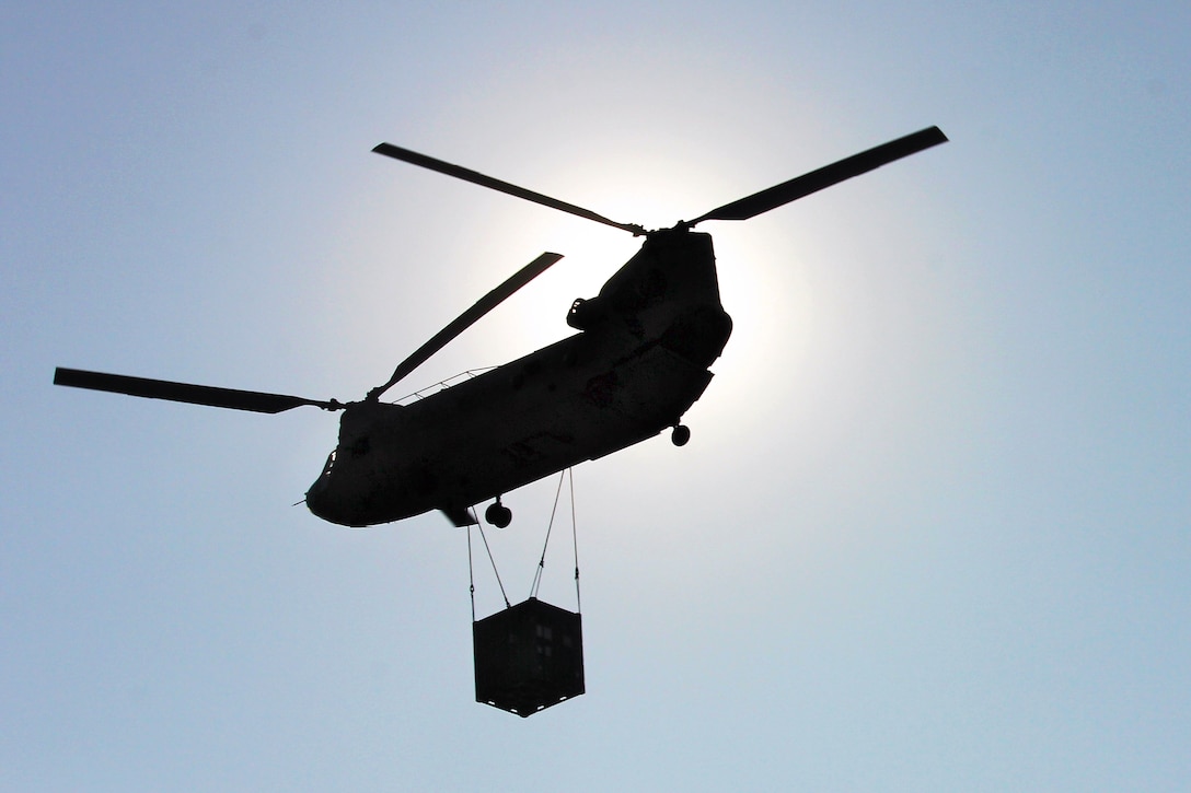 A CH-47 Chinook helicopter takes off with a shipping container during ...