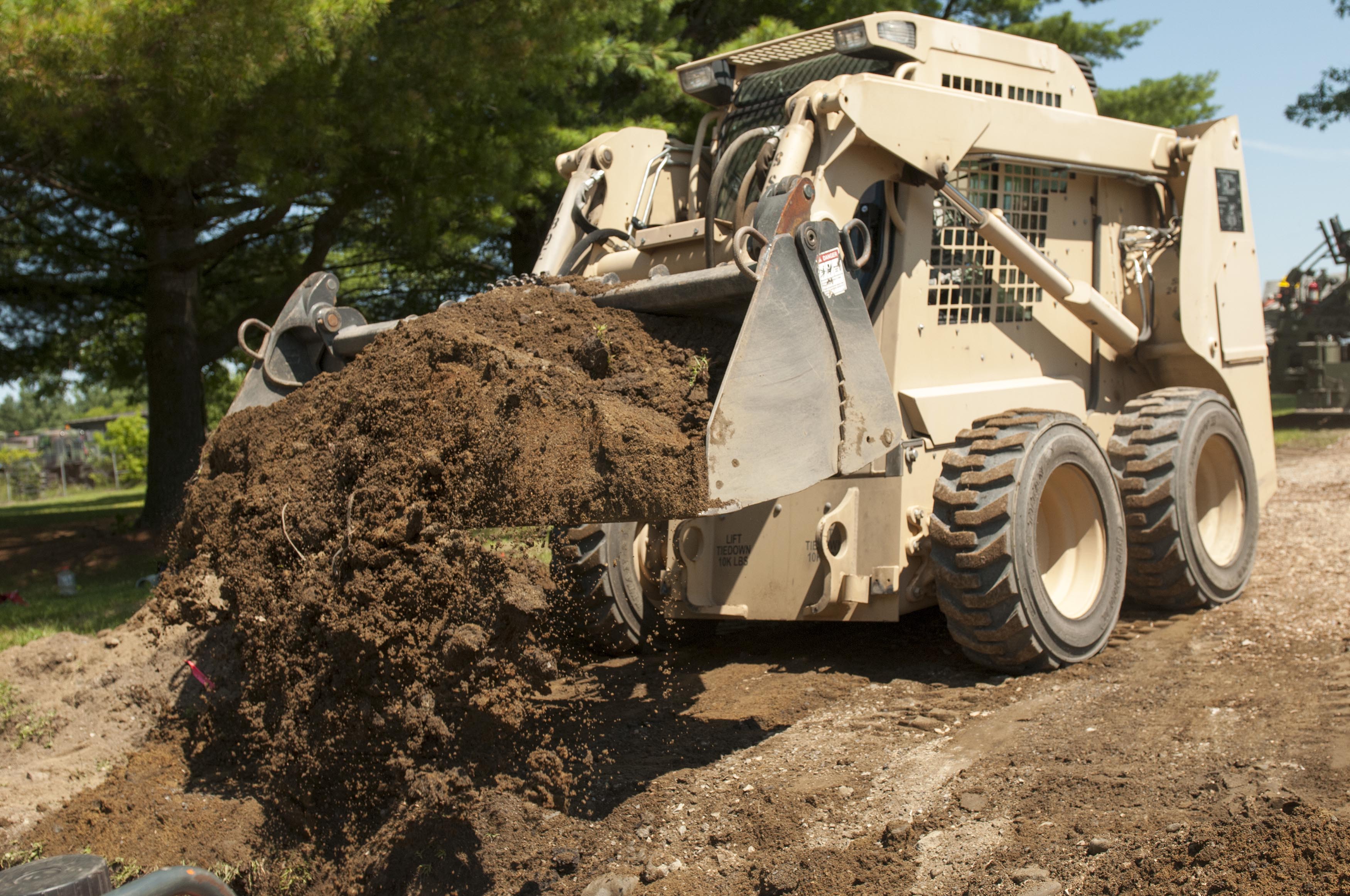 A soldier uses a skid-steer loader to bury a polyvinyl chloride, or PVC ...