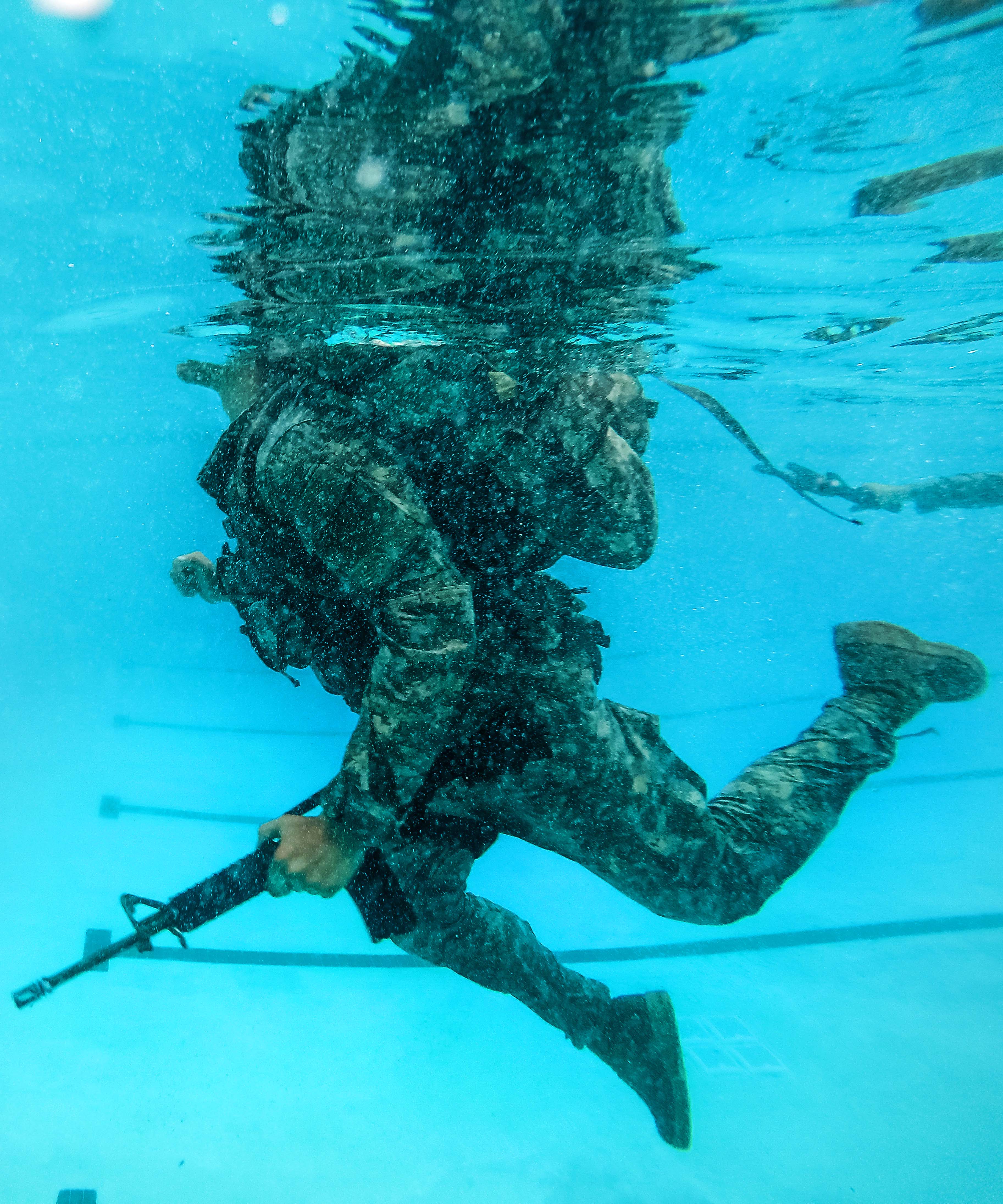A soldier swims 25 meters with a ruck sack and a dummy weapon during ...