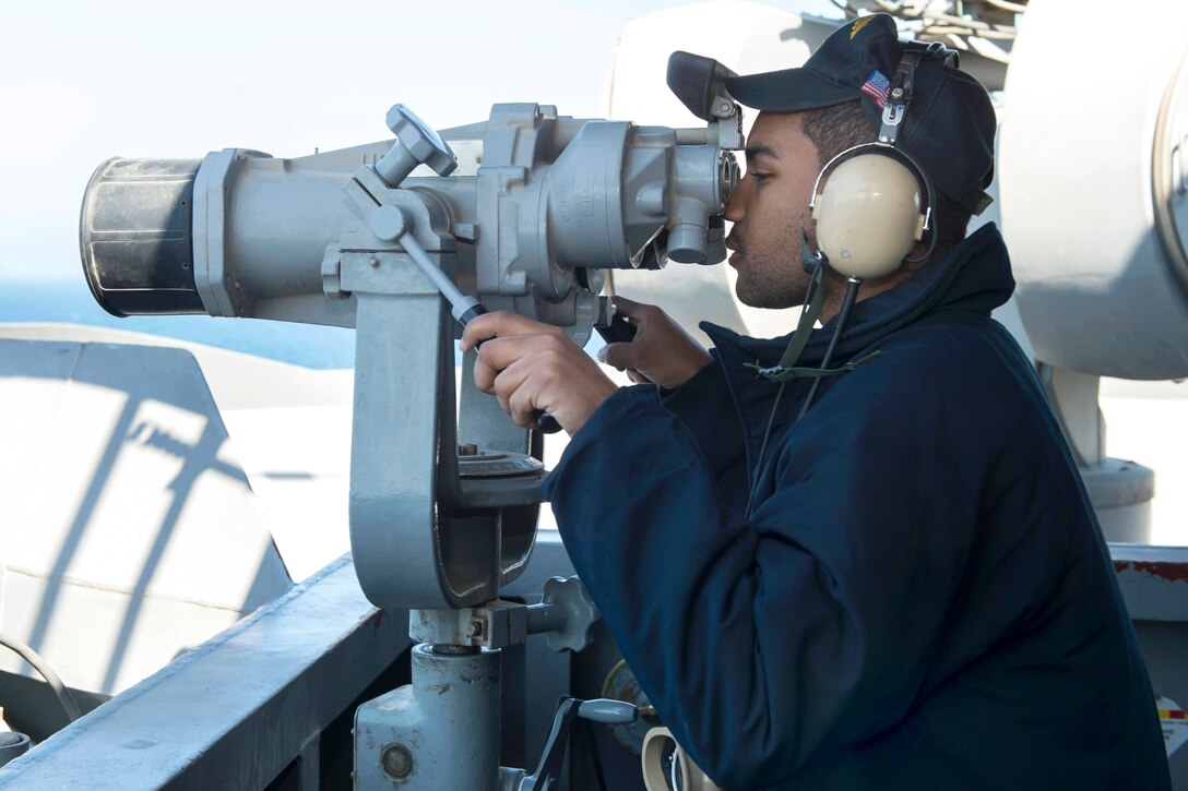 U.S. Navy Seaman Eric Taylor uses high-powered binoculars to scan the ...